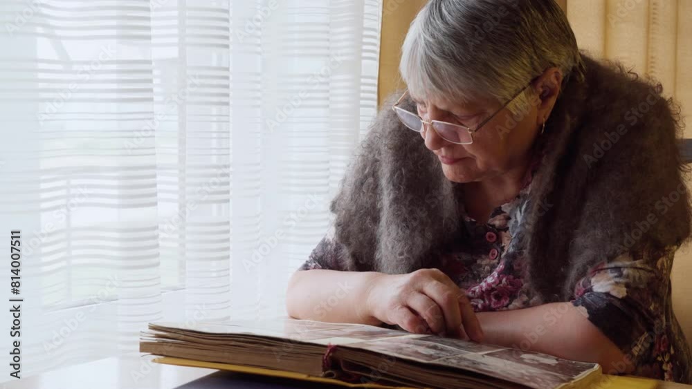 A 70-year-old elderly woman looks through photos from a family album ...