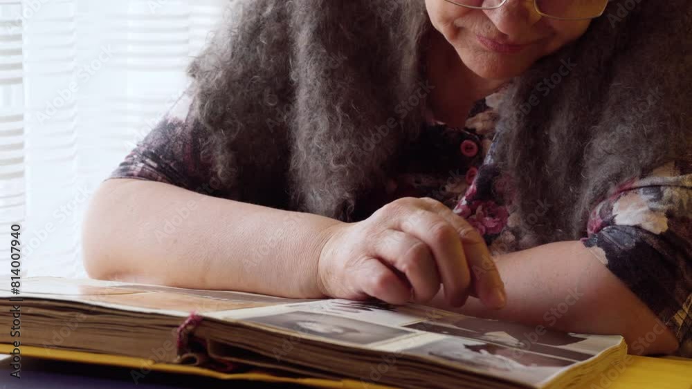 A 70-year-old elderly woman looks through photos from a family album ...