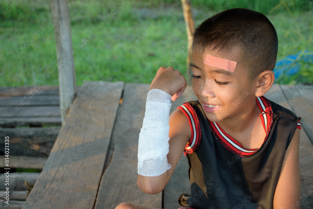 Asian boy smiling shows wounds on his arm and head and bandages them ...