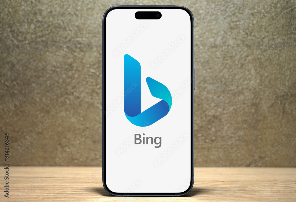 Bing logo is displayed on a modern smartphone standing on a desk ...