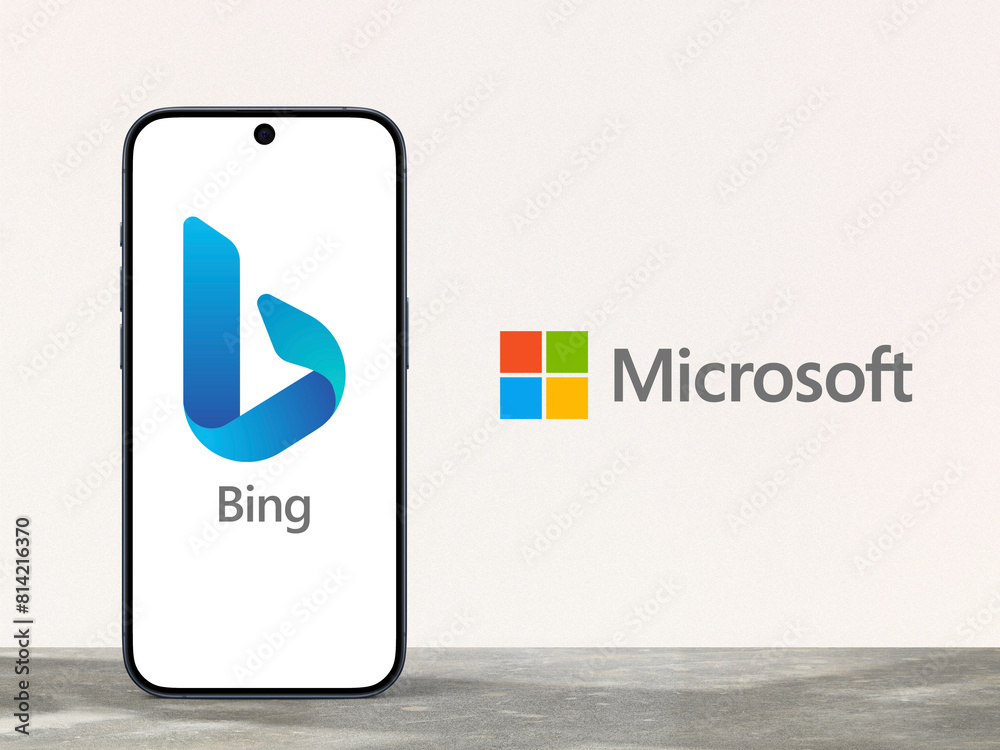 Bing logo is displayed on a modern smartphone standing on a desk ...