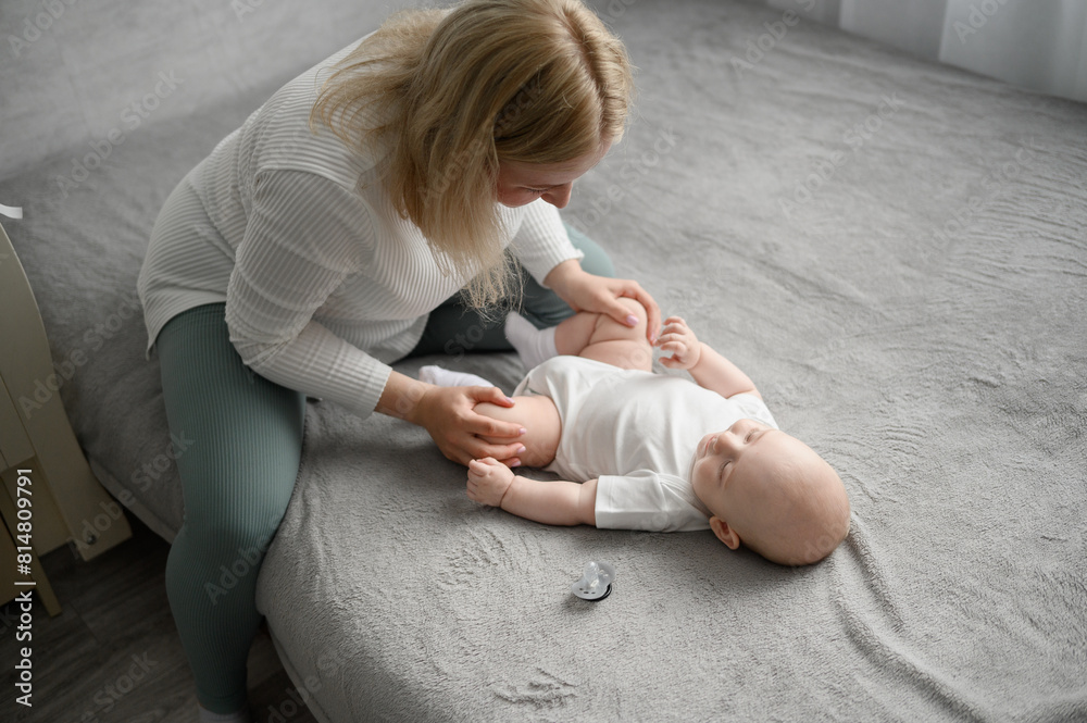 Baby lies on bed at home, mom does morning exercises for infant ...