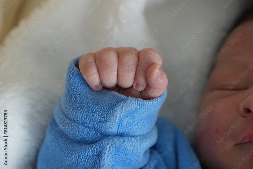 A detailed shot of a newborn baby's clenched hand, wrapped in a blue ...