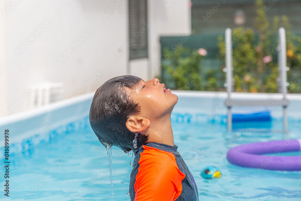 Boy in a pool tilts his head back, water cascading down, refreshing ...