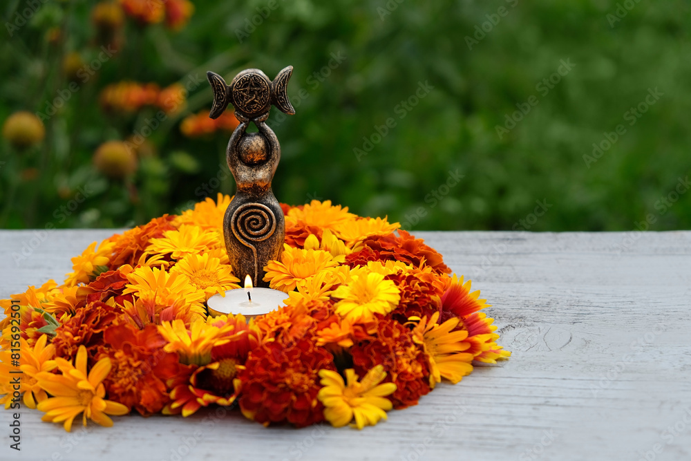 Triple Goddess figurine with candle and colorful flowers on table in ...