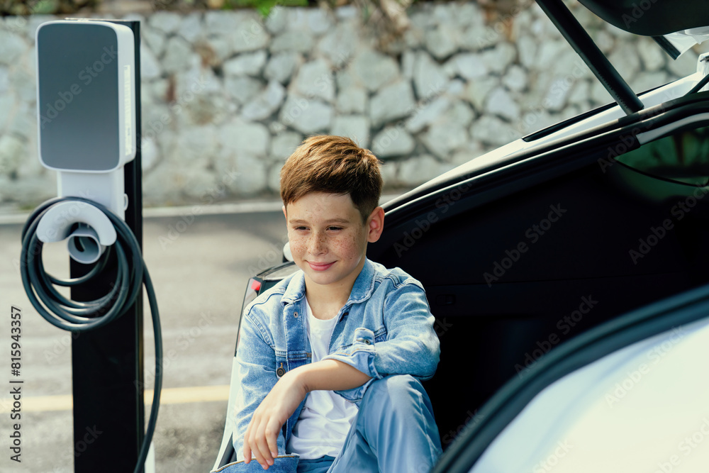 Little boy sitting on car trunk while recharging eco-friendly electric ...