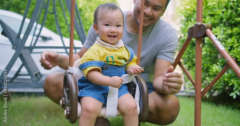 A joyful moment of a father pushing his smiling baby in a swing at a ...