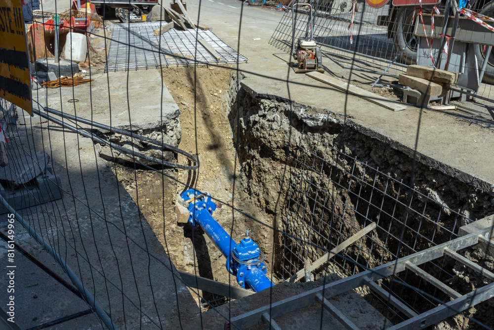 An open trench on a construction site with blue pipe, metal fence, and ...