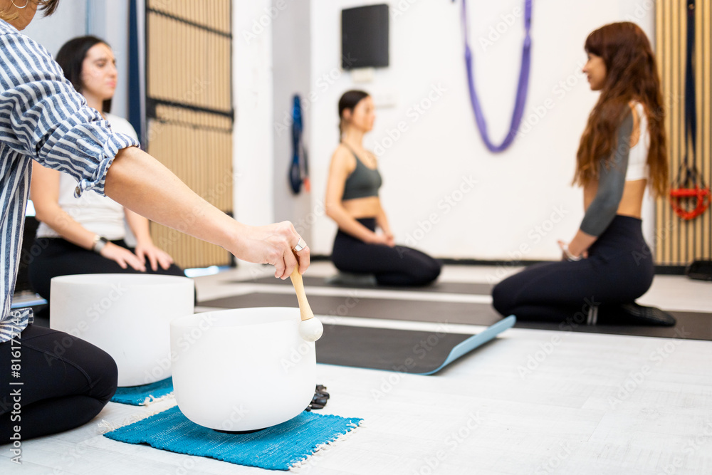 A group of women are in a sound bath class inside a room. The ...