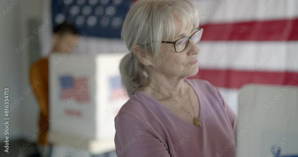 Senior woman with hair up, thinking while casting votes at booth with ...