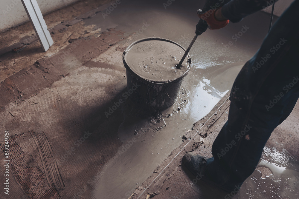 Worker mixing concrete in bucket indoors. Man is mixing spackling paste ...