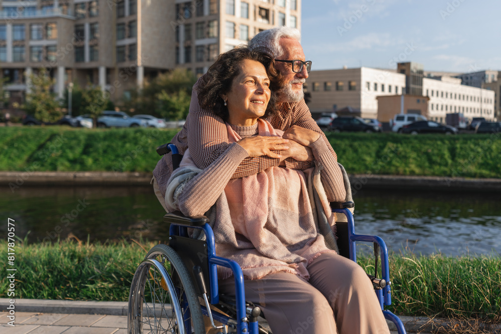 Senior woman in wheelchair walking with caregiver old man on road in ...