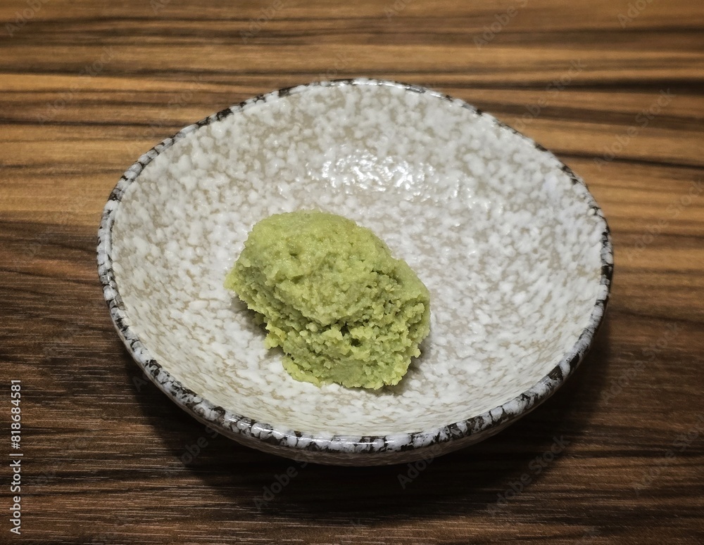 Wasabi in a small white ceramic dish is used mixed with soy sauce to be ...