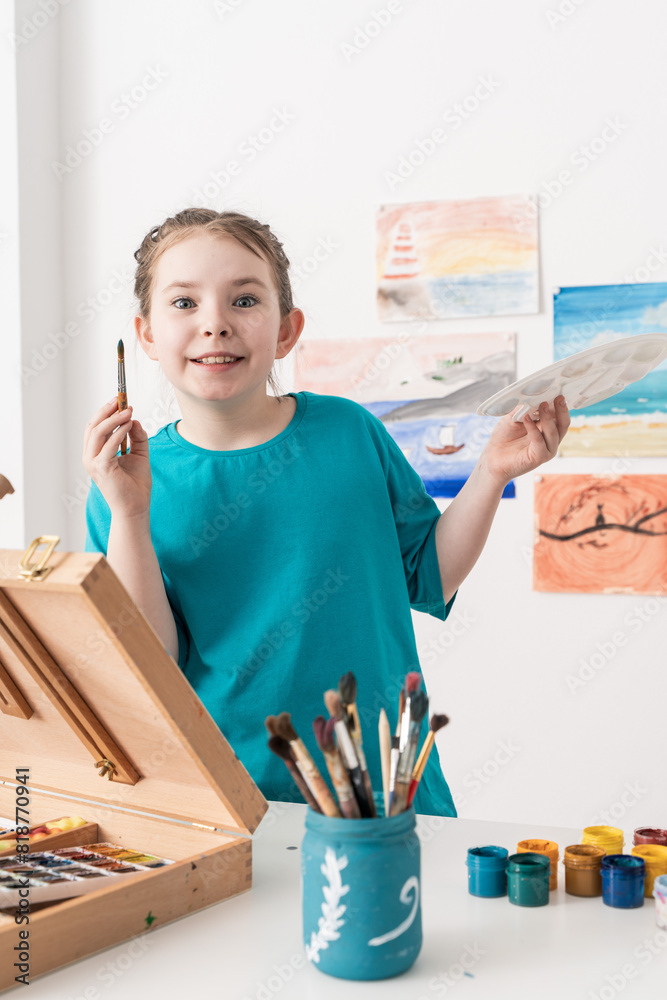 Cute little girl painting with brush and paints with easel and palette ...