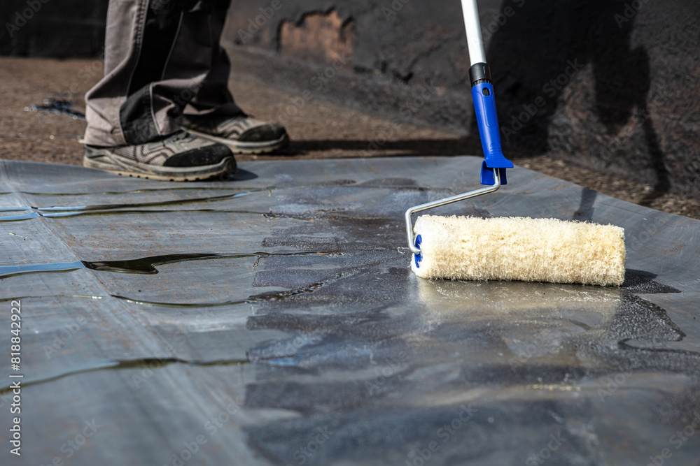 man applies adhesive to an old bitumen sealant and then glues on a ...