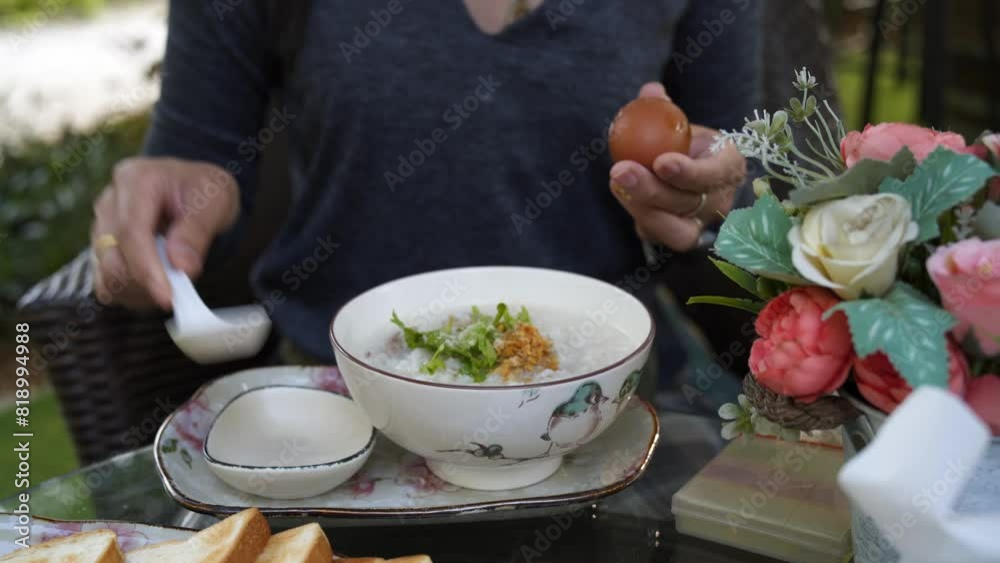 Asian woman cracks soft-boiled eggs into lump pork porridge on a clear ...