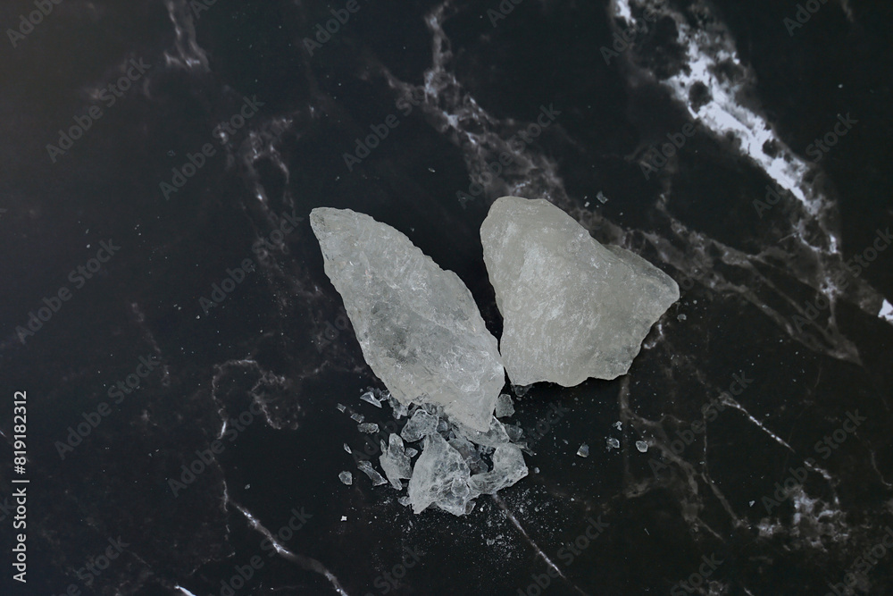Lumps of alum on a black background. It is a mineral with clear, white ...