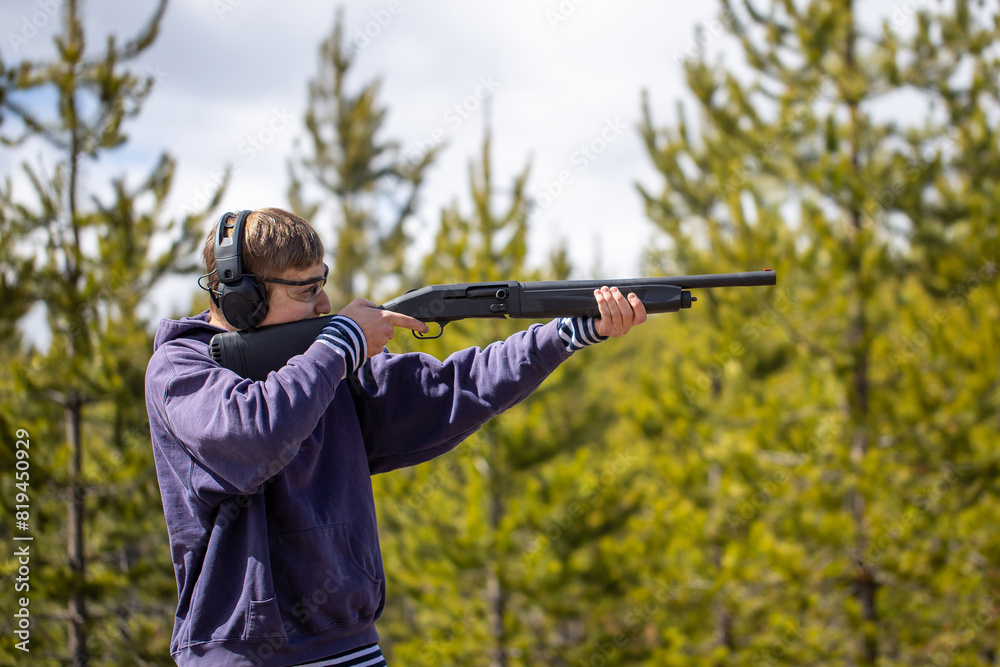 Static image of a young man shooting shotgun in the forest. Side view ...