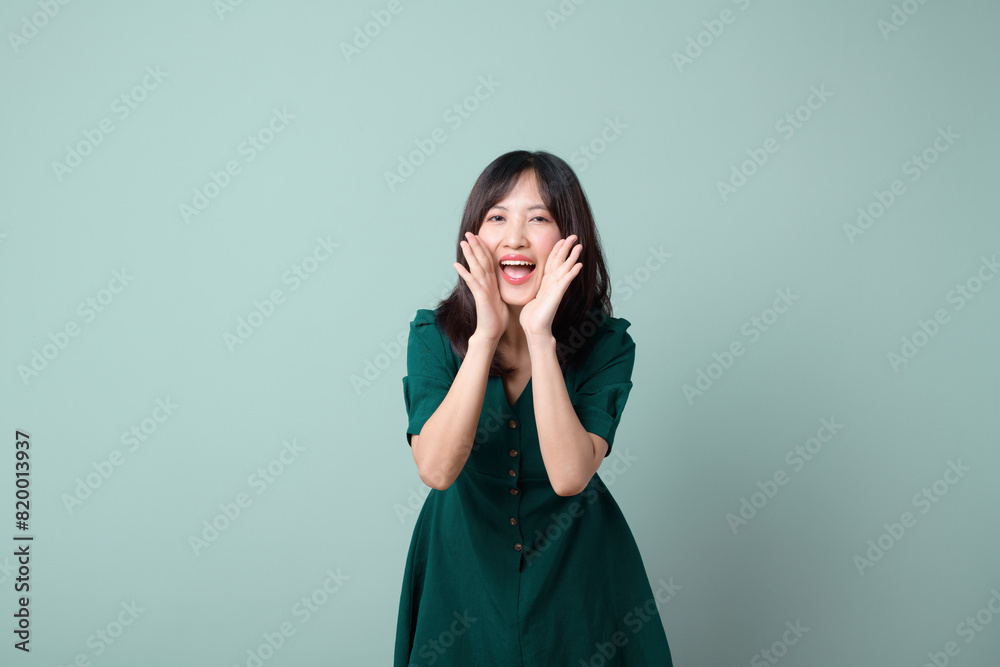 Happy Asian woman shouting above green dress poses against green ...