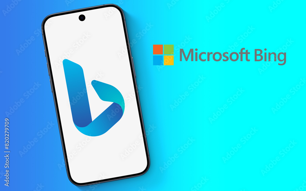 Bing logo is displayed on a modern smartphone laying on a blue gradient ...