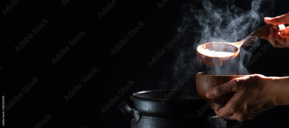 The cook is cooking rice porridge in a boiling clay pot with steam ...