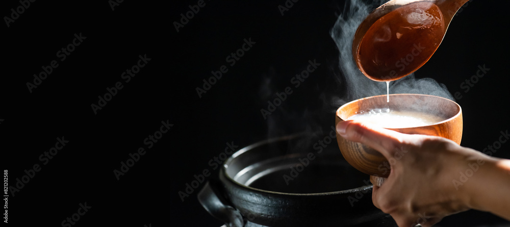 The cook is cooking rice porridge in a boiling clay pot with steam ...