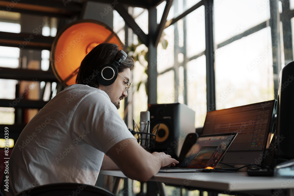 Man working on an audio project in a home studio, wearing headphones ...