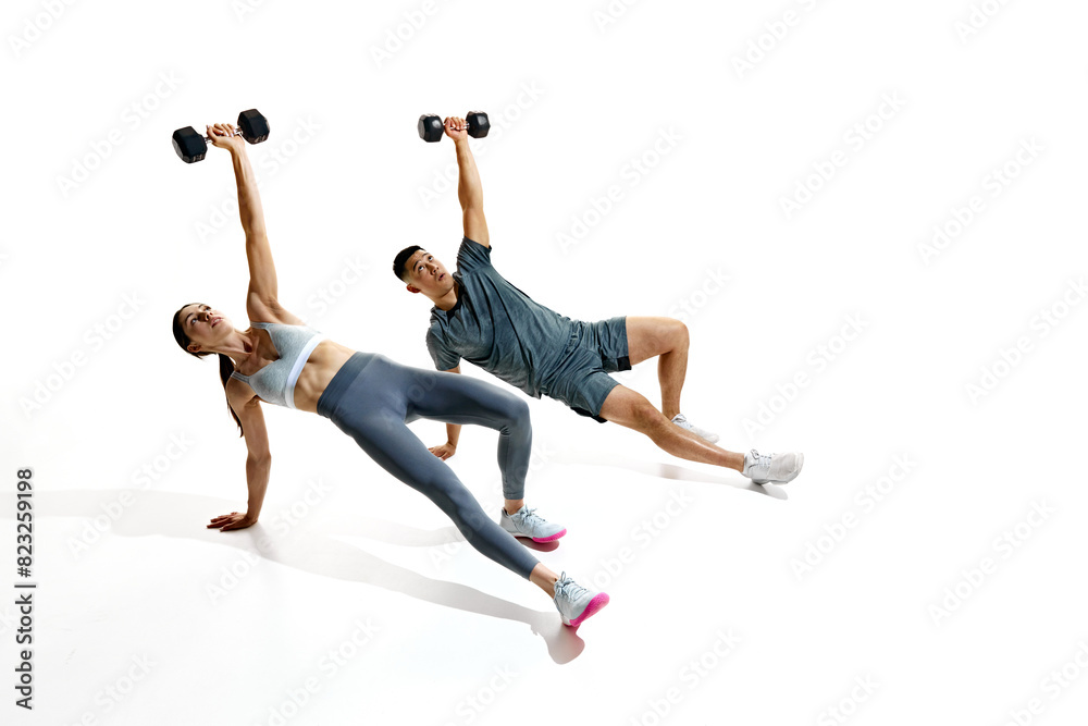 Athletic man and woman performing challenging exercise with dumbbells ...