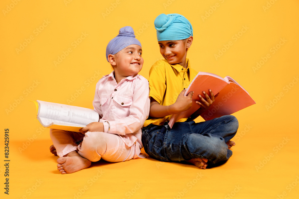 Two Happy indian sikh school kids sitting on floor holding note books ...