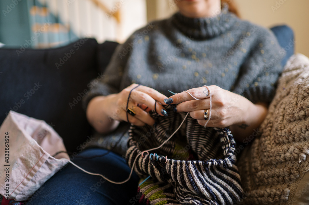 woman relaxing at home on sofa and knitting with two strands of yarn ...