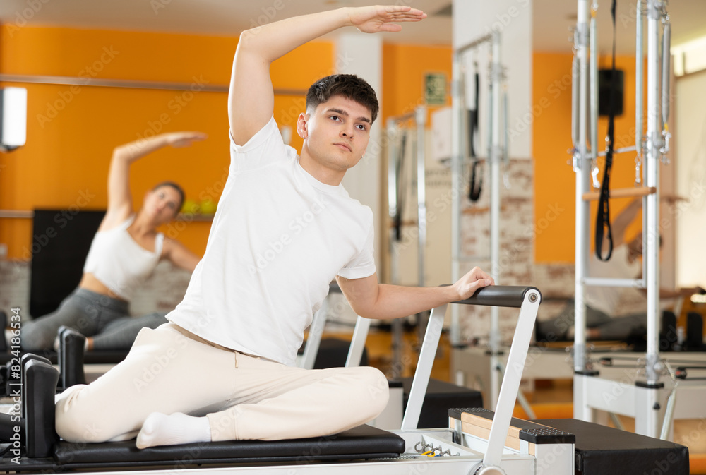 Focused young guy practicing Pilates on reformer in brightly colored ...