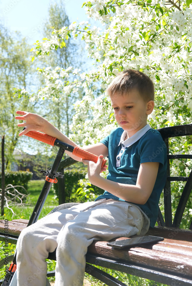 Boy is crying alone in park on bench, sitting and sad because of broken scooter. Child broke toy ...