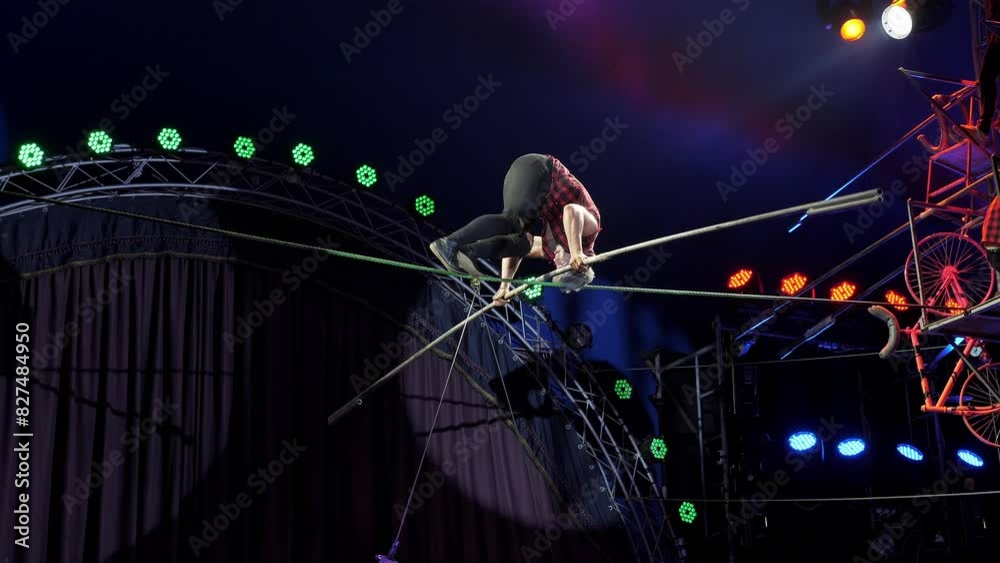 An acrobat with a stick stands on his head on a tightrope under the ...