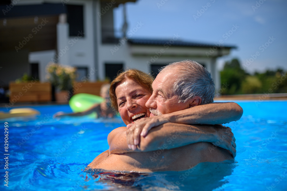 Couple of cheerful seniors shaving fun in pool with friends jumping ...