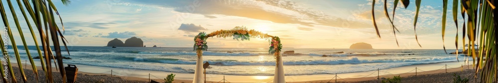 A beach wedding setup with an arch decorated with flowers, facing the ...