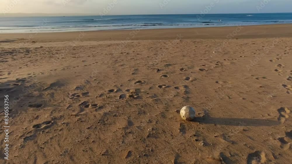 an old scruffy soccer ball rolling along beach sand with tire imprints ...