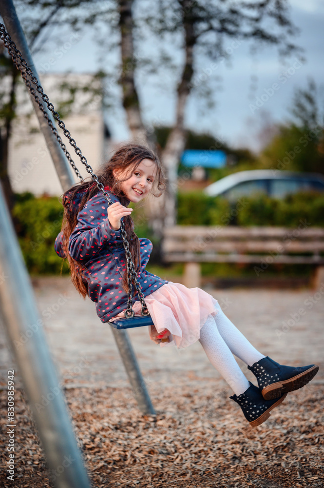 Smiling young girl with long hair, wearing a blue polka dot jacket and pink skirt, enjoys ...