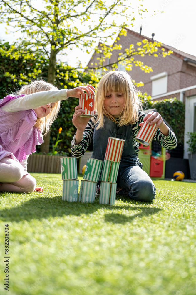 Two children are playing with colorful blocks on a grassy lawn, with ...