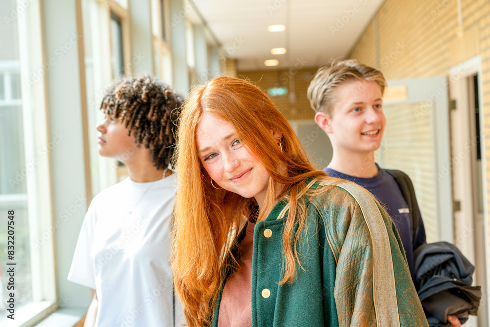 Three students standing in a school corridor, smiling and posing for ...
