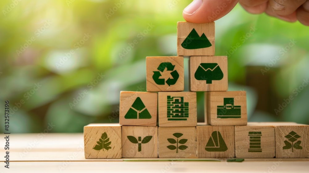 The photo shows a hand arranging wooden blocks with green icons ...