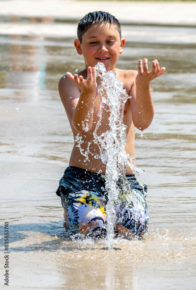 Young boy relaxes in a urban splash pad, as he plays in the cool water ...