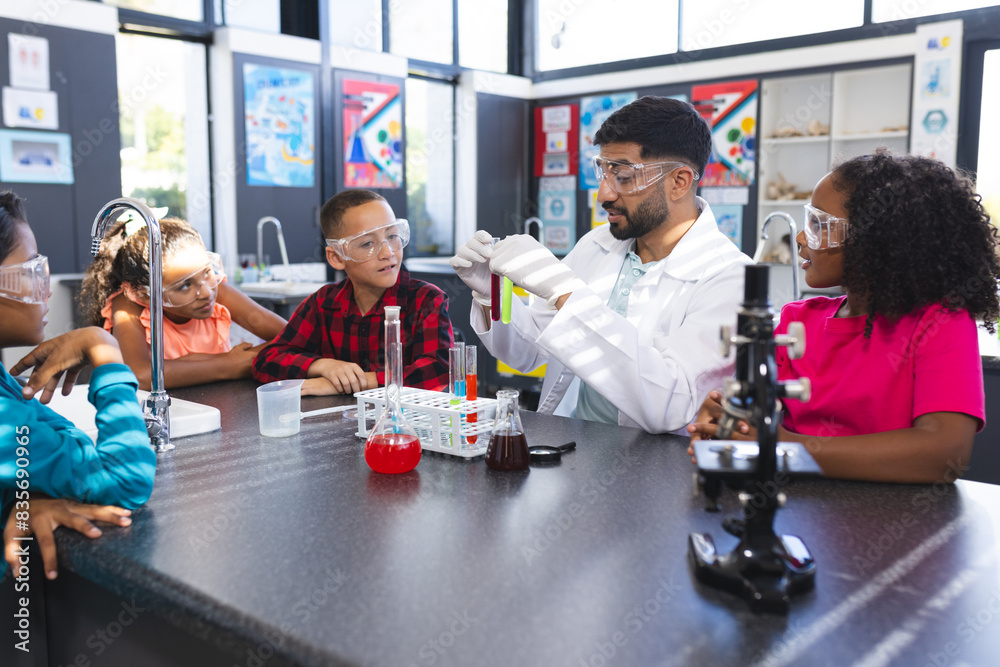 Asian male teacher shows test tube to three biracial students during ...
