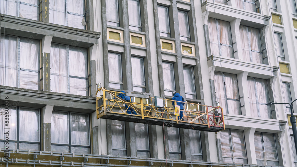 Workers in a construction cradle at a height perform installation work ...