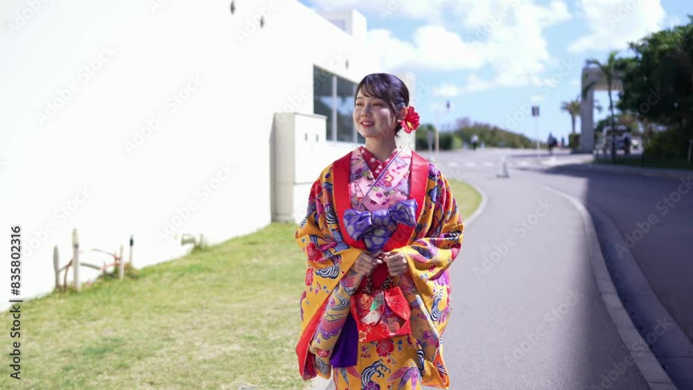 A young woman in her twenties, wearing traditional Ryusou, is walking outdoors in Okinawa. Her ...