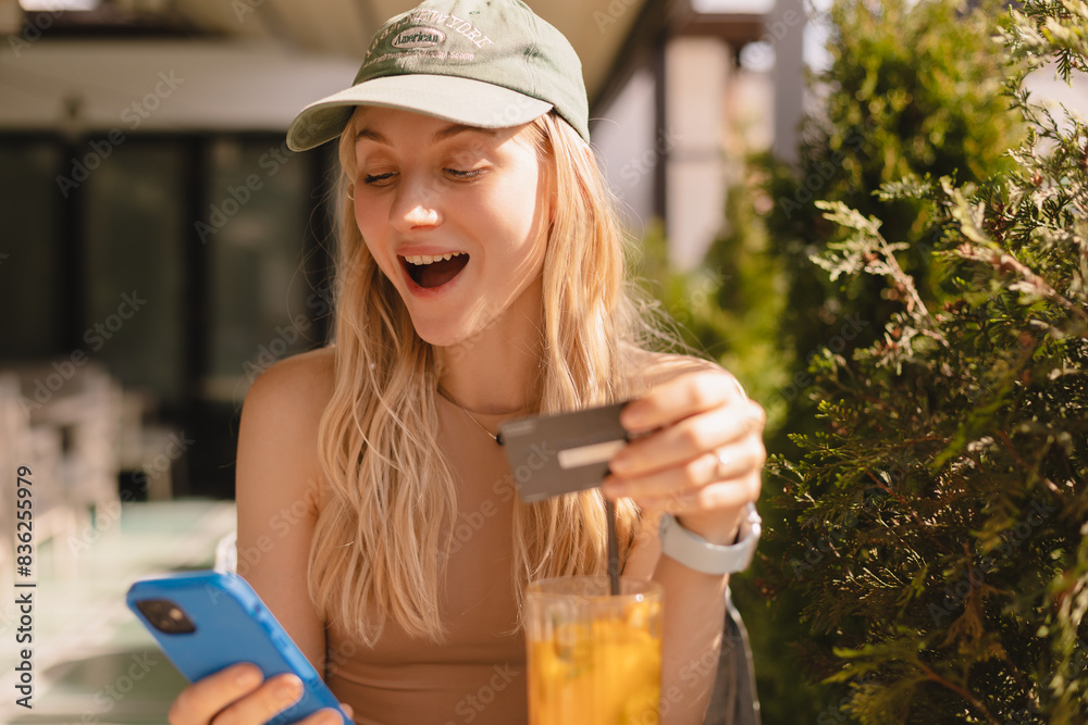 Shocked blonde lady holding credit card and smartphone, looking at ...