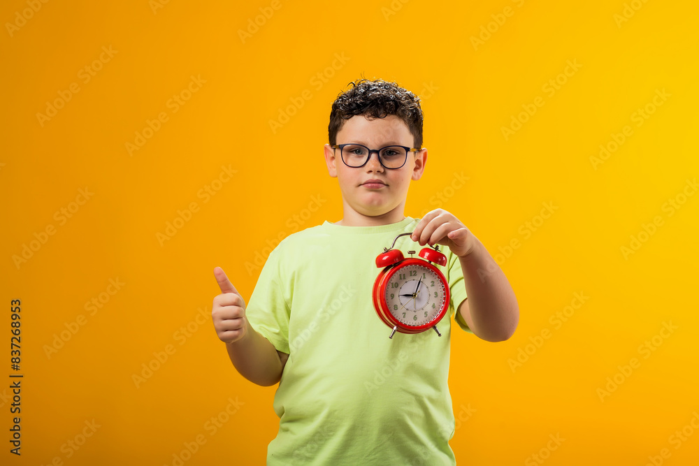 Child boy holding alarm clock and showing thumb up gesture over yellow ...