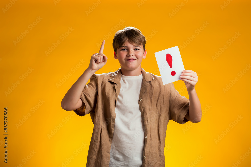 Surprised boy holding exclamation point card and showing finger up ...