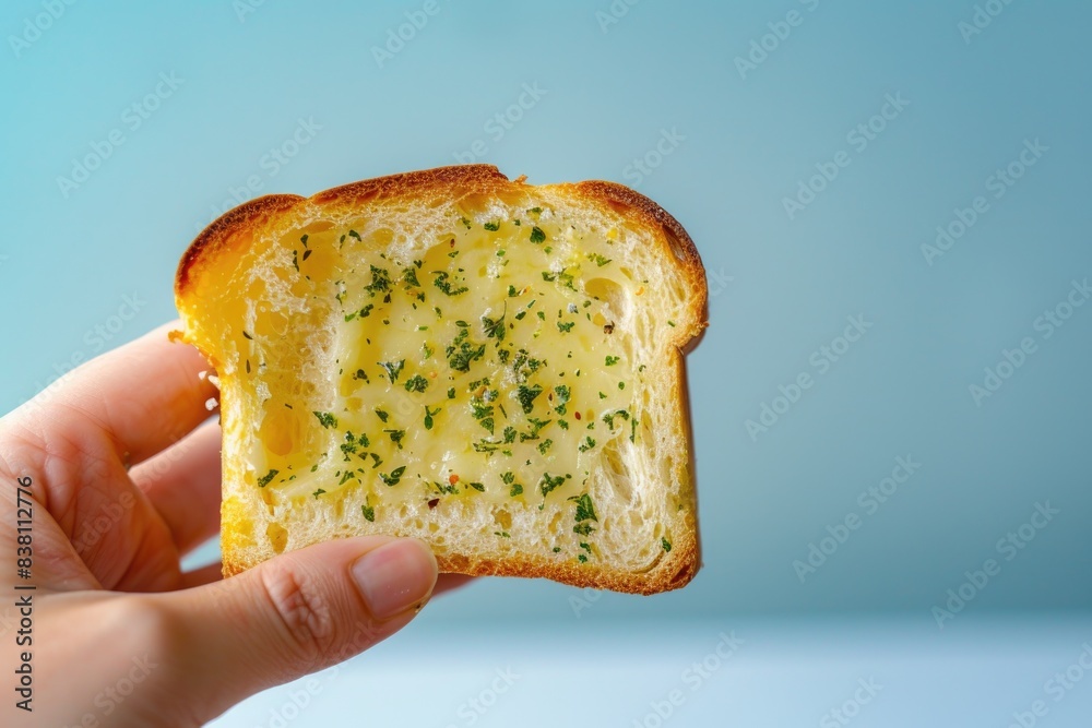 hand holding a slice of garlic bread, focus on the buttery texture ...