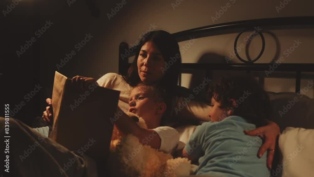 Girl reading bedtime story to her brother with their mother by their ...