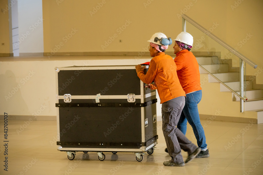 Two workers pushing a flightcase to set up a stage in an auditorium ...